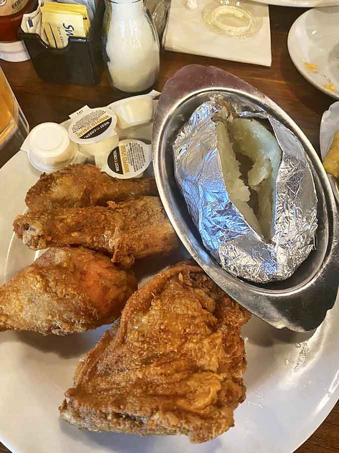 Southern fried chicken with that perfect golden crunch, alongside a baked potato wrapped like a precious gift – comfort food royalty on a plate.