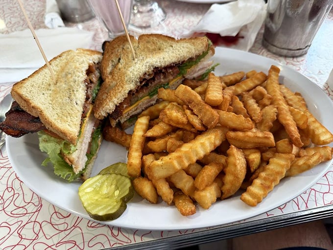 The classic club sandwich stands tall and proud, a triple-decker monument to the art of sandwich construction, flanked by golden crinkle-cut sentinels.