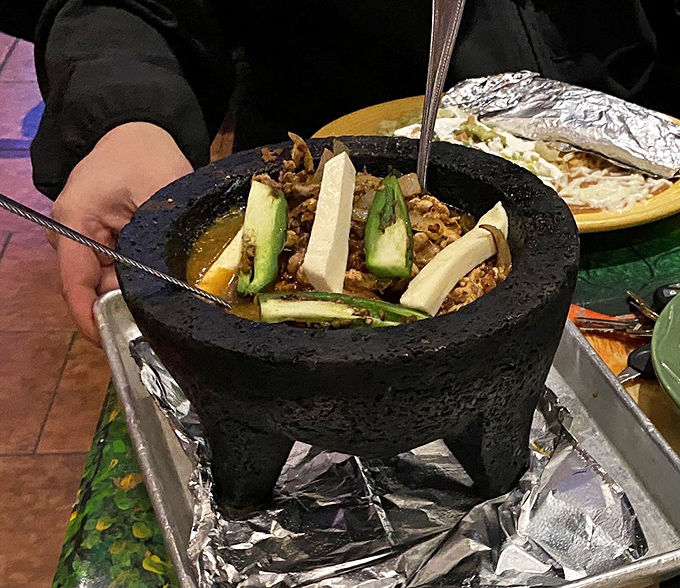 The molcajete isn't just dinner, it's dinner theater – a volcanic stone cauldron bubbling with savory treasures that turns heads as it crosses the dining room.