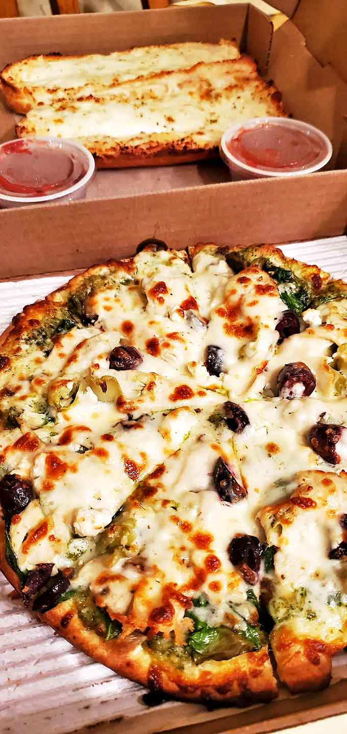 The pesto pizza replaces traditional red sauce with vibrant basil pesto, topped with fresh tomatoes and dollops of creamy cheese that melt into edible art.