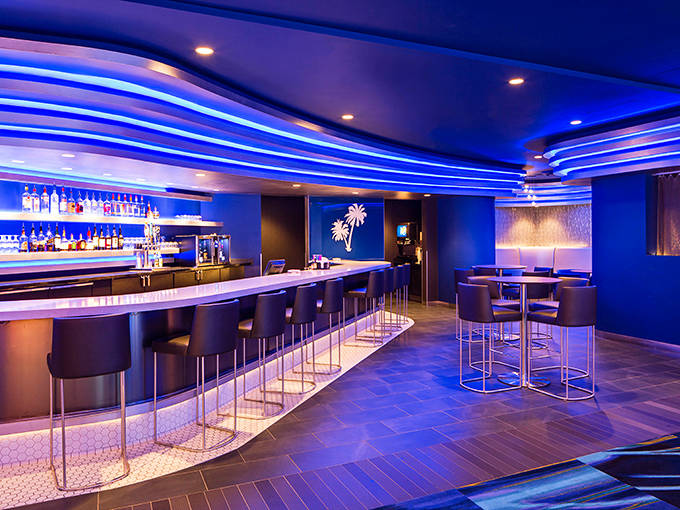 The sleek bar area glows with electric blue ambiance, promising sophisticated adult refreshment after conquering the water slides.