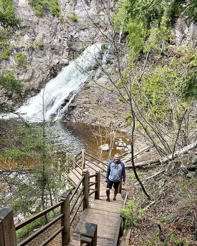 A hiker ascends the wooden staircase, each step revealing more of the waterfall's majesty. The perfect reward system: climb, then be amazed.