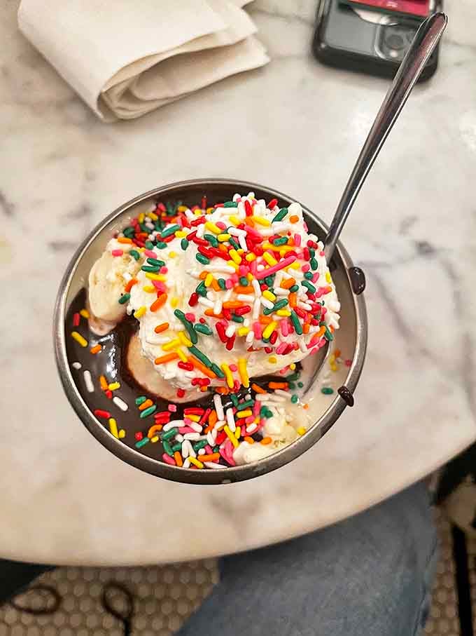 Rainbow sprinkles add a carnival of color to this classic sundae &ndash; proof that sometimes happiness is just ice cream and jimmies.