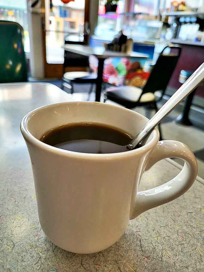 A sturdy white mug sits quietly, offering the promise of honest coffee — simple, comforting, and free from fancy names or elaborate preparation.