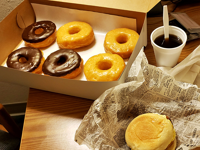 Morning indulgence done right: chocolate glaze meets golden donut while glazed companions wait their turn beside a steaming coffee.