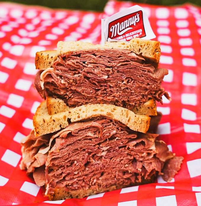 The legendary pastrami sandwich sits proudly on its checkered throne, meat stacked higher than some downtown parking garages.