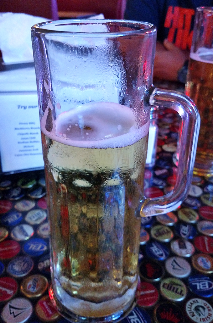 A frosty mug of beer on that signature bottle cap table &ndash; the ideal wing wingman for your flavor journey.