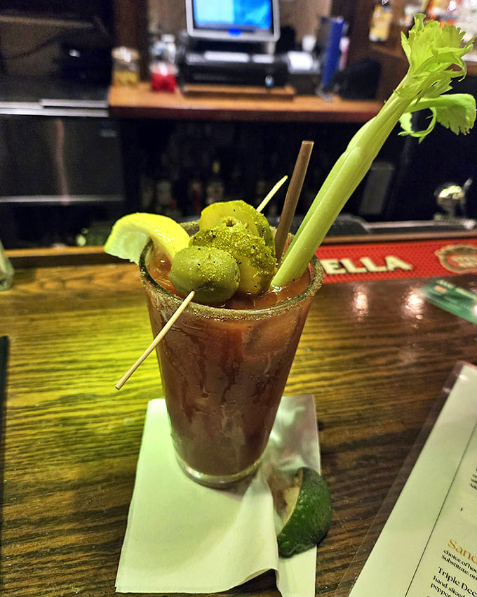 The Bloody Mary arrives like a liquid appetizer, garnished with enough accessories to qualify as both cocktail and small meal.