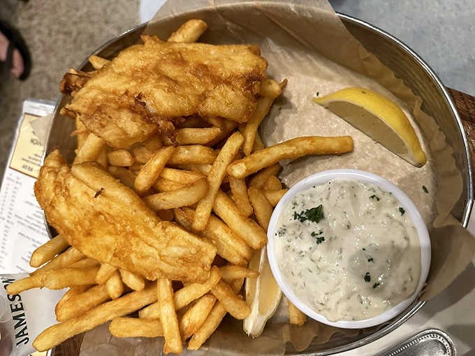 Golden-battered cod rests atop a mountain of chips, accompanied by house-made tartar sauce &ndash; the quintessential British takeaway, elevated.