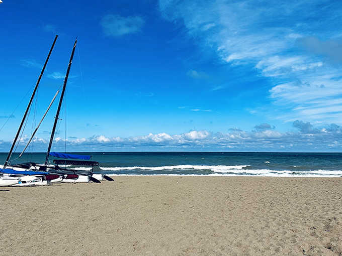 Colorful sailboats rest on golden sand, patiently waiting for adventure-seekers to harness the lake's reliable afternoon breezes.