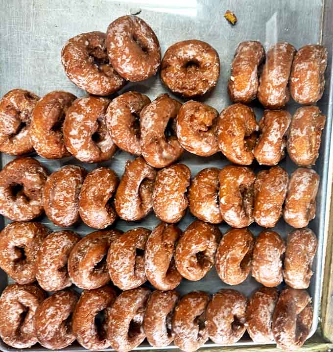 Chocolate-glazed donuts lined up like sweet soldiers, their perfect uniformity suggesting decades of practiced craftsmanship.