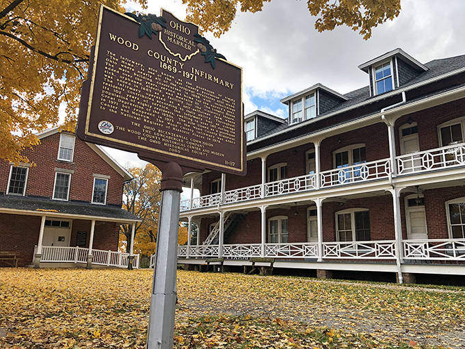 Autumn leaves create a golden carpet around the historic Wood County Infirmary, where brick walls have witnessed over a century of community evolution.