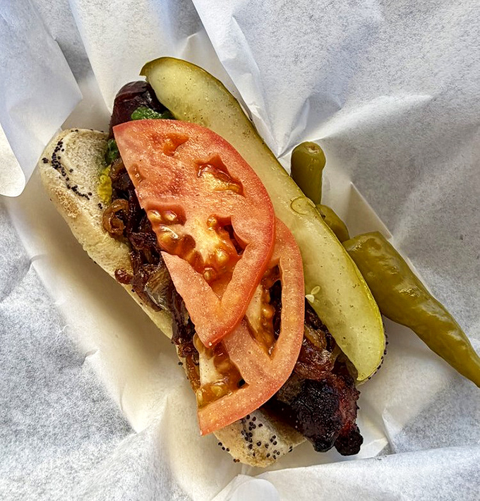 The Char Polish &ndash; a split, char-grilled sausage with that perfect snap, adorned with fresh tomato, pickle, and sport peppers.