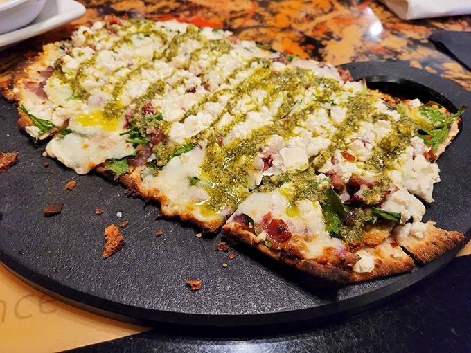 The flatbread presents as a minimalist masterpiece, where creamy cheese and vibrant pesto create striking contrasts against the crisp crust.