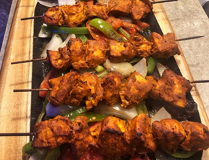 Chicken shish kebabs grilled to charred perfection, resting on a bed of colorful peppers and onions &ndash; simple food executed with obvious care.
