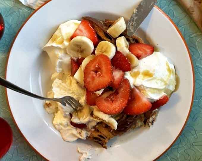 A mountain of cinnamon-raisin French toast topped with fresh strawberries, bananas, and whipped cream &ndash; breakfast that doubles as dessert without a hint of guilt.