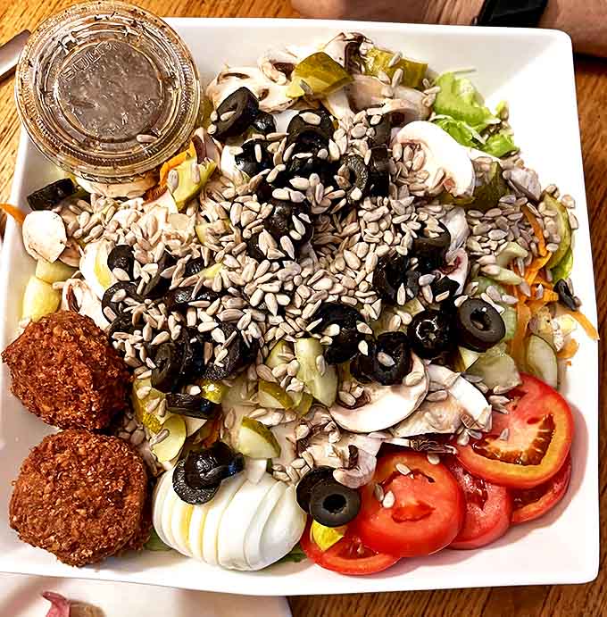 Falafel Salad: A vibrant garden on a plate featuring Tommy's famous falafel, fresh vegetables, olives, and sunflower seeds &ndash; healthy eating never looked so appealing.