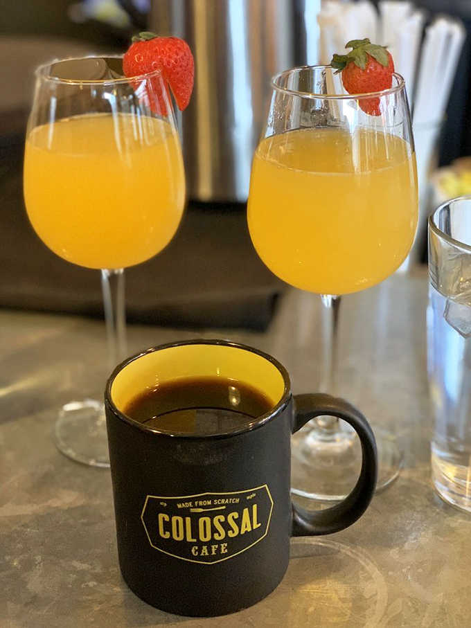 Morning decisions made easy: robust coffee in a branded mug alongside mimosas garnished with fresh strawberries, because sometimes you need both.