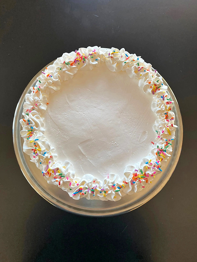 "Over the Rainbow" isn't just a cake &ndash; it's a circular canvas of white frosting artistry, where sprinkles dance along the edges like colorful confetti.