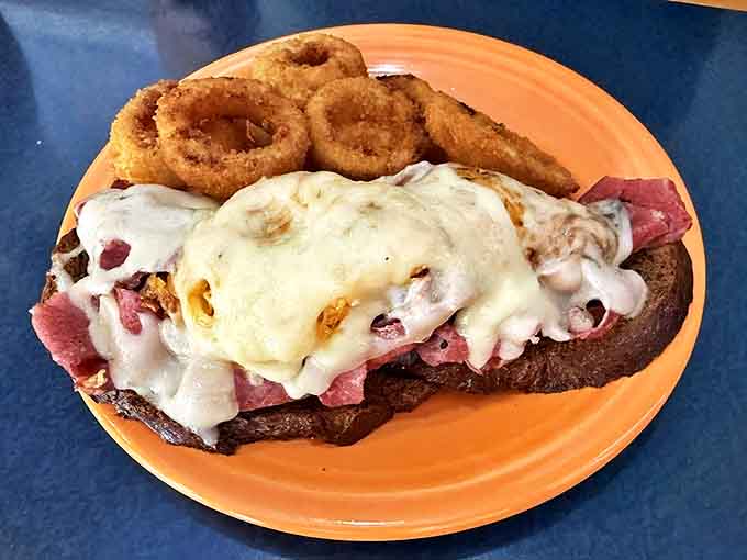The Reuben sandwich in all its melty, meaty glory, flanked by golden onion rings that shatter with each delicious bite.