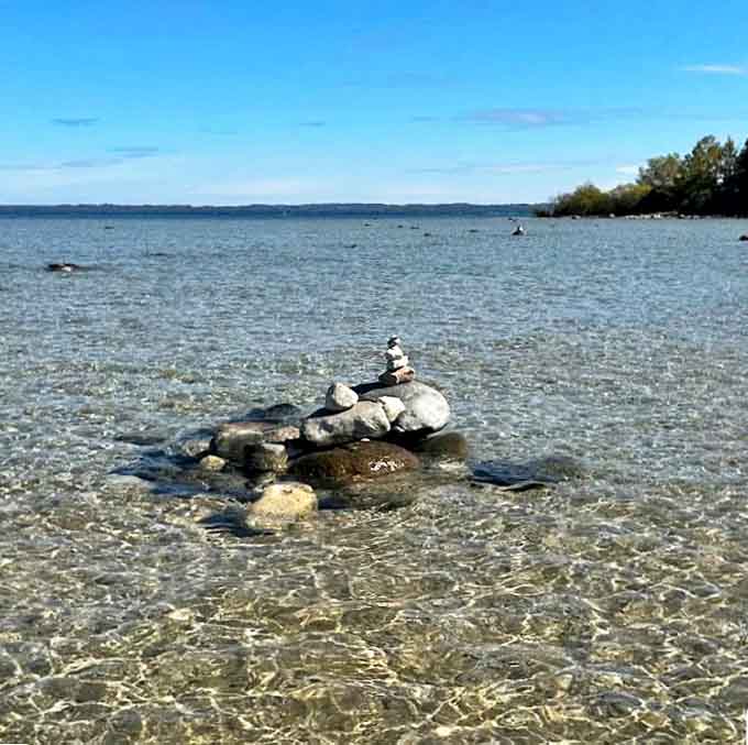 Balanced stones emerge from crystal-clear waters, temporary monuments created by visitors leaving their mark on this timeless shoreline.