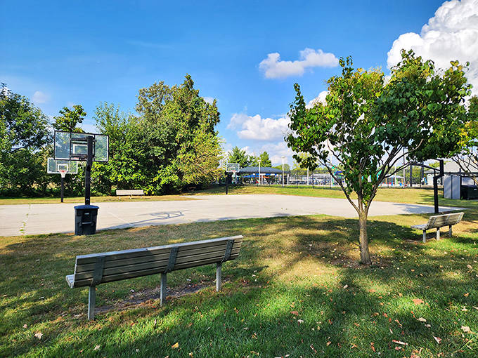 This peaceful park bench offers the perfect vantage point for watching impromptu basketball games or simply soaking in the simple pleasures of outdoor leisure.