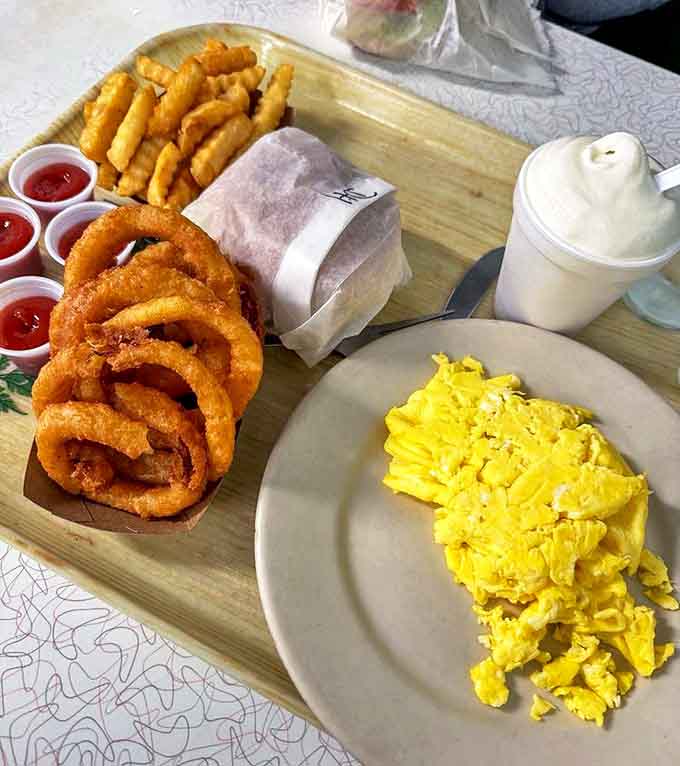 The breakfast-lunch confusion plate &ndash; golden eggs, crispy onion rings, and crinkle-cut fries creating the perfect anytime comfort meal.