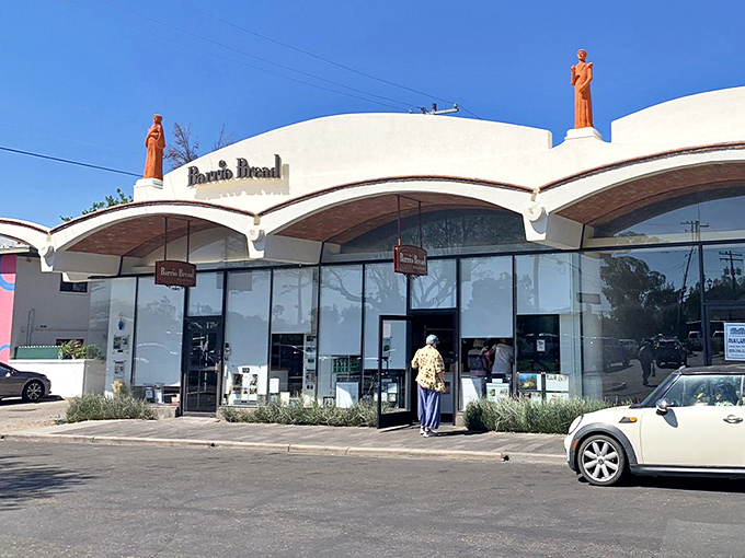 Barrio Bread's distinctive white stucco exterior with terracotta statues standing guard, a Tucson landmark that promises carb-laden treasures within.