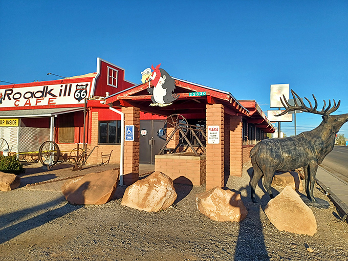 The iconic red exterior of Roadkill Cafe welcomes hungry travelers with its cartoon buzzard mascot and metal elk guardian.