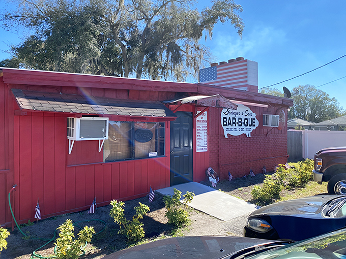 The iconic red exterior of Granger & Sons stands proudly under Florida skies, promising smoky delights within. American flag included&mdash;because patriotism tastes delicious.
