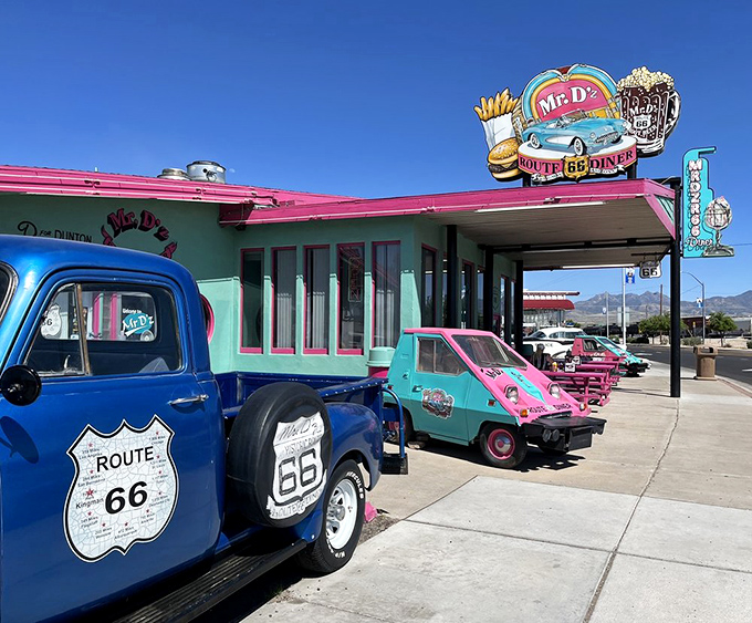 A splash of turquoise and pink welcomes hungry travelers, with vintage vehicles standing guard at this Route 66 landmark.