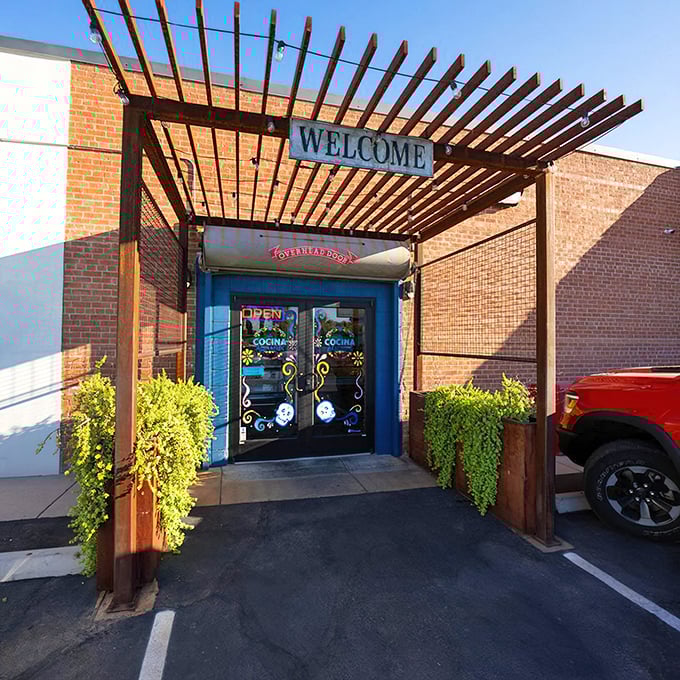 A welcoming wooden pergola frames the entrance to Cocina Adamex, where culinary adventures await behind those vibrant blue doors.