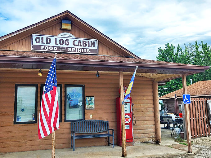 The rustic wooden exterior of Old Log Cabin welcomes travelers with its vintage charm and proudly displayed American flag &ndash; a true Route 66 landmark.