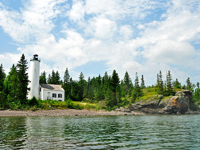 A classic white lighthouse stands sentinel against Lake Superior's blue waters, surrounded by dense forest – Michigan's maritime heritage preserved.