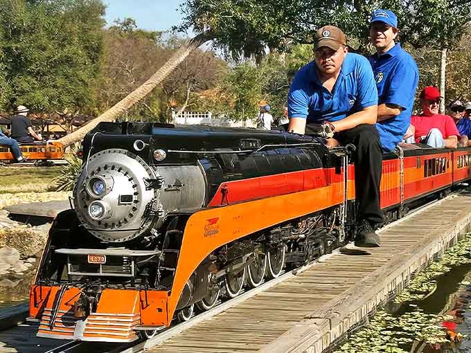 A gleaming orange and black miniature locomotive pulls passenger cars along wooden tracks &ndash; childhood dreams realized in perfect 1/8 scale.