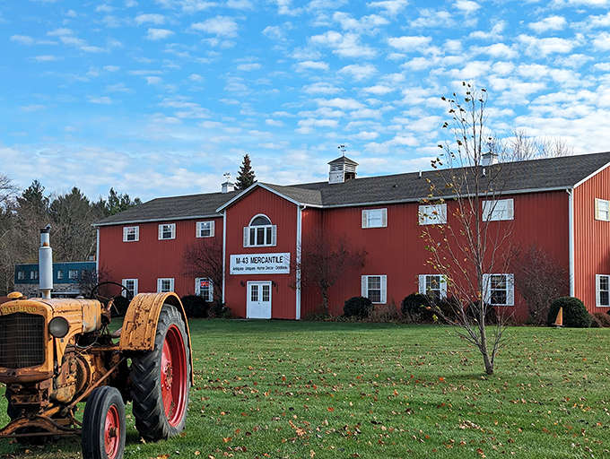 The classic red barn exterior of M-43 Mercantile stands proudly against Michigan's blue sky, complete with vintage farm equipment guarding the entrance.