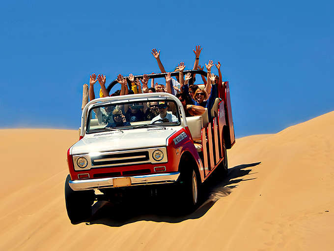 Thrill-seekers with arms raised high, riding the sandy rollercoaster of Mac Wood's Dune Rides – Michigan's answer to "who needs theme parks anyway?"