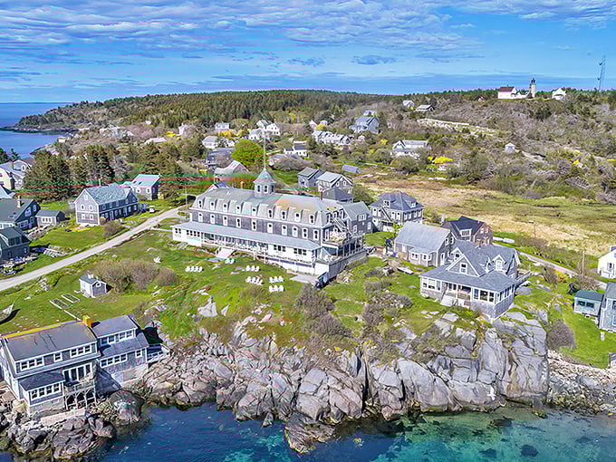 A postcard-perfect aerial view showcasing the iconic Island Inn perched dramatically on granite cliffs, with fishing boats dotting the protected harbor below.