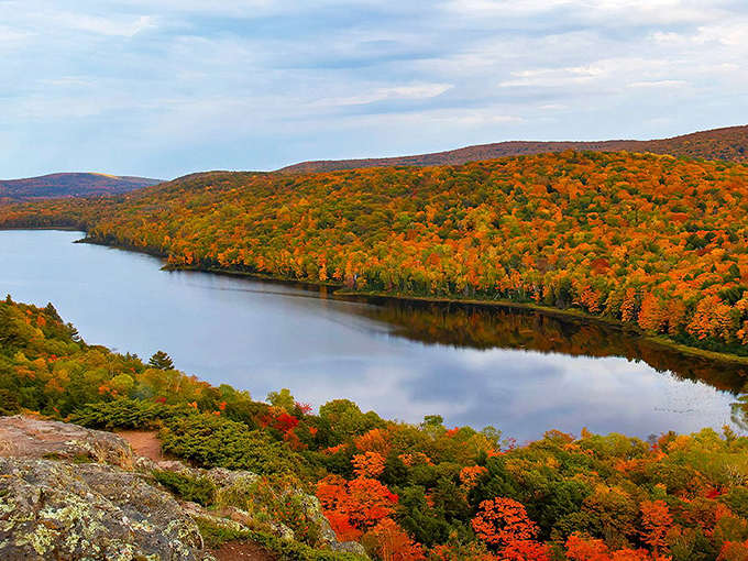 Nature's masterpiece unfolds at Porcupine Mountains Wilderness State Park, where autumn paints the landscape in fiery hues reflected perfectly in the serene lake below.