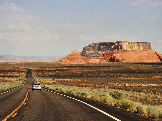 State Route 98 stretches toward the horizon like a black ribbon, with majestic red buttes standing sentinel against an impossibly blue Arizona sky.