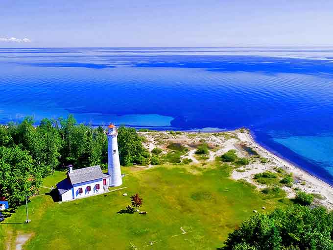 Sturgeon Point Lighthouse stands tall against Lake Huron's endless blue horizon, its white tower gleaming like a beacon of welcome to all who visit.