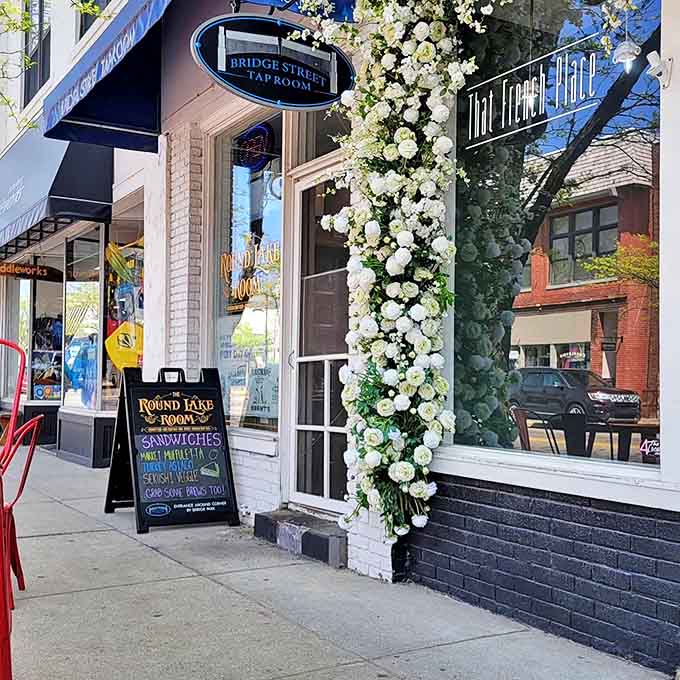 The charming exterior of That French Place, where cascading white flowers frame the entrance like nature's own welcome mat to pastry paradise.