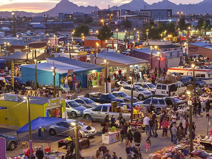 Aerial view of the Tanque Verde Swap Meet at dusk, with the Catalina Mountains creating a dramatic backdrop as shoppers navigate the maze of colorful vendor stalls.