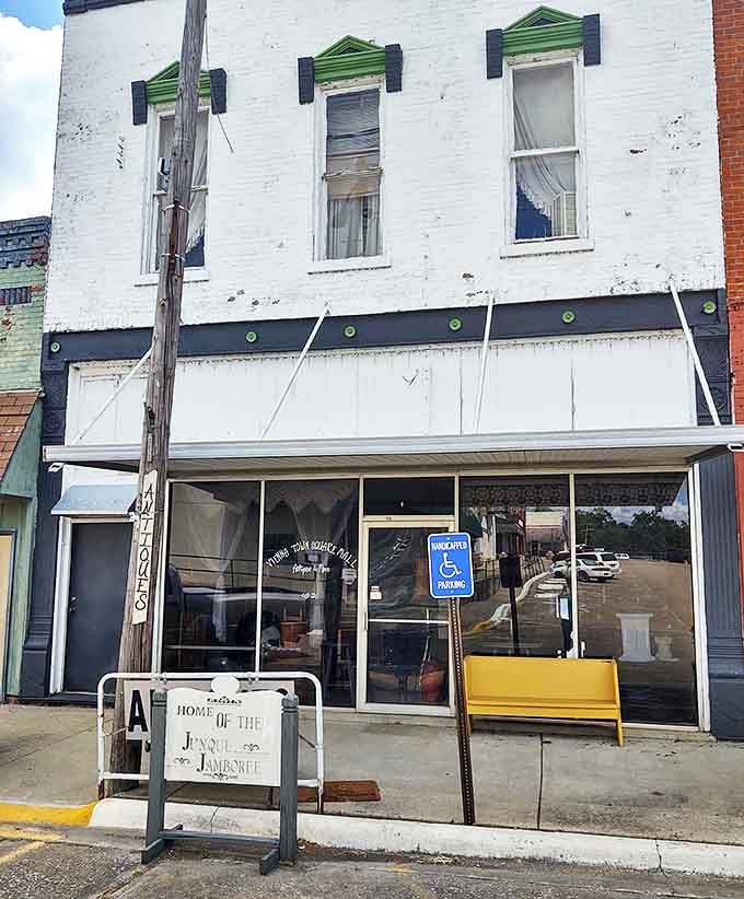 A humble white brick storefront with green-trimmed windows stands as a portal to the past, promising treasures beyond its unassuming facade.