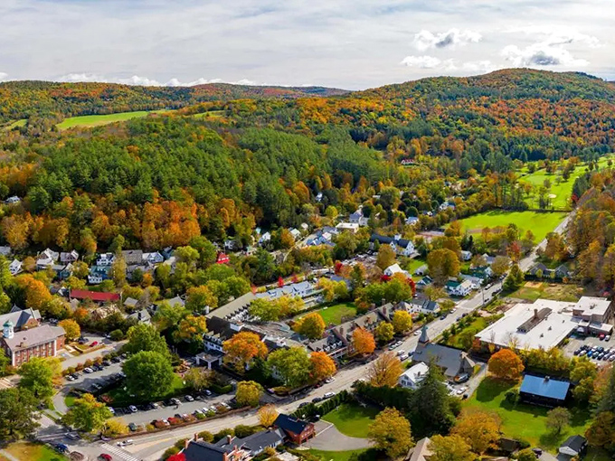 Woodstock Town: A bird's-eye view of Vermont's most photogenic town, where fall foliage creates a patchwork quilt of fiery colors surrounding historic white buildings.
