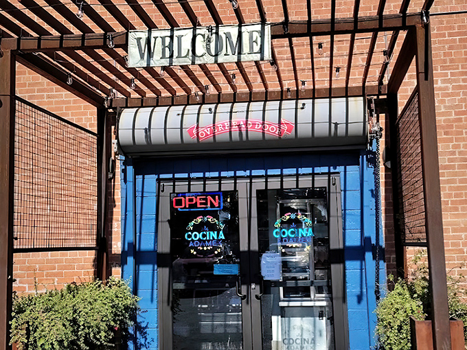 The welcoming entrance to Cocina Adamex beckons with its vibrant blue doors and rustic wooden pergola – a colorful portal to flavor paradise.