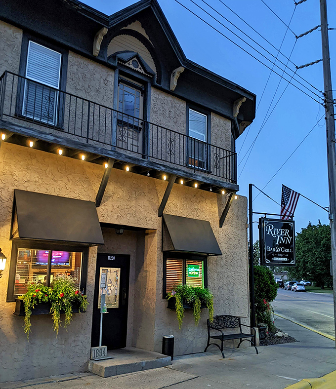 The stucco exterior of River Inn Bar & Grill welcomes visitors with charming hanging plants and warm lighting, a humble facade hiding culinary treasures within.