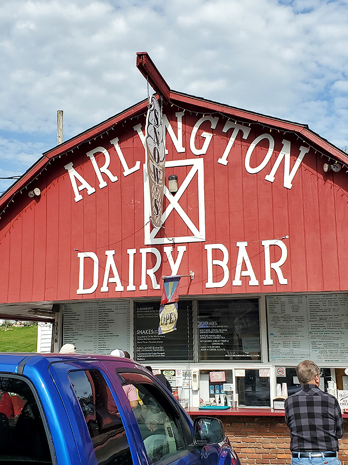 The iconic red barn facade of Arlington Dairy Bar stands proudly against Vermont's sky, promising delicious memories with every visit.