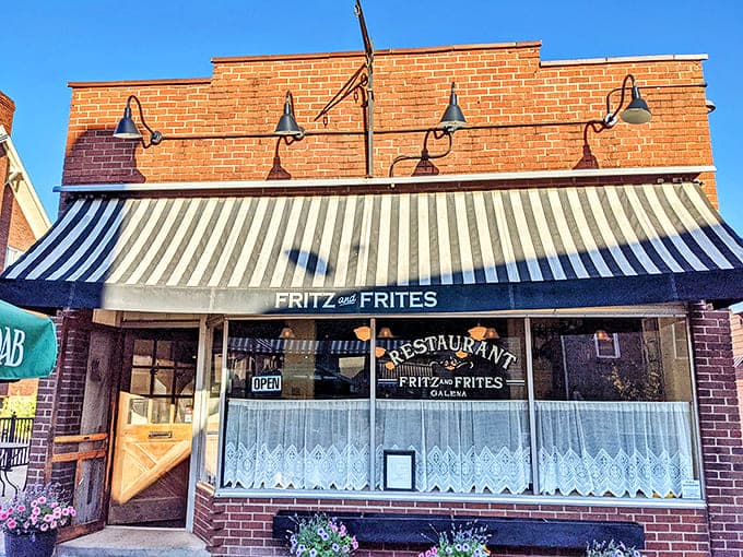 The charming brick exterior of Fritz and Frites beckons with its classic striped awning and warm lighting, promising European delights within.