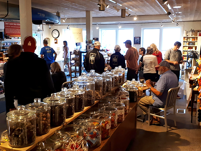 Shoppers gather among rows of candy jars and local goods, creating a lively, bustling Hero&rsquo;s Welcome moment.